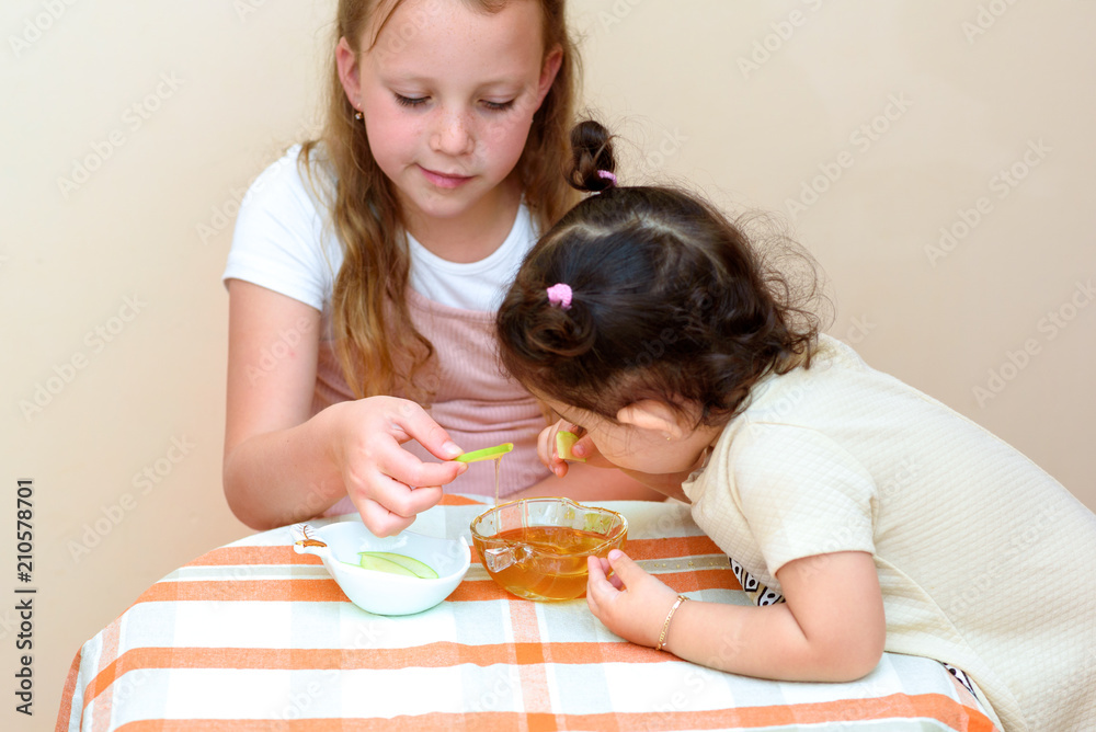 Close up portrait of two funny cute little girl eat apple with honey ...