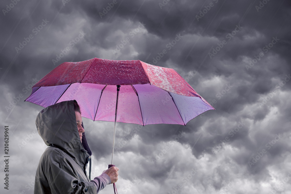 Woman with an umbrella against the background of a dark stormy sky. The ...