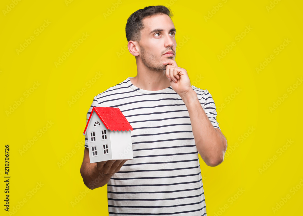 Handsome real estate agent holding a house serious face thinking about ...