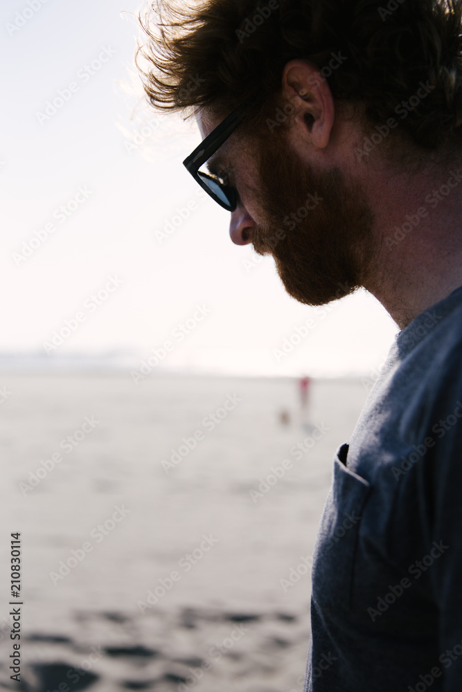 Red bearded man with sunglasses on a beach during golden hour seen from ...