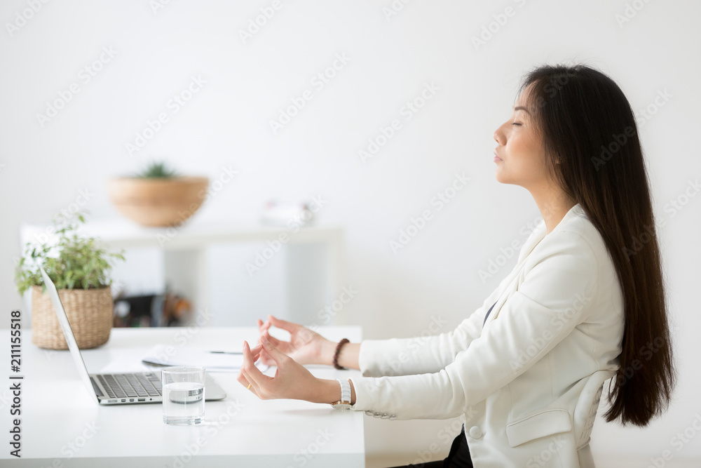 Calm thoughtful Asian female employee sitting at office desk meditating ...