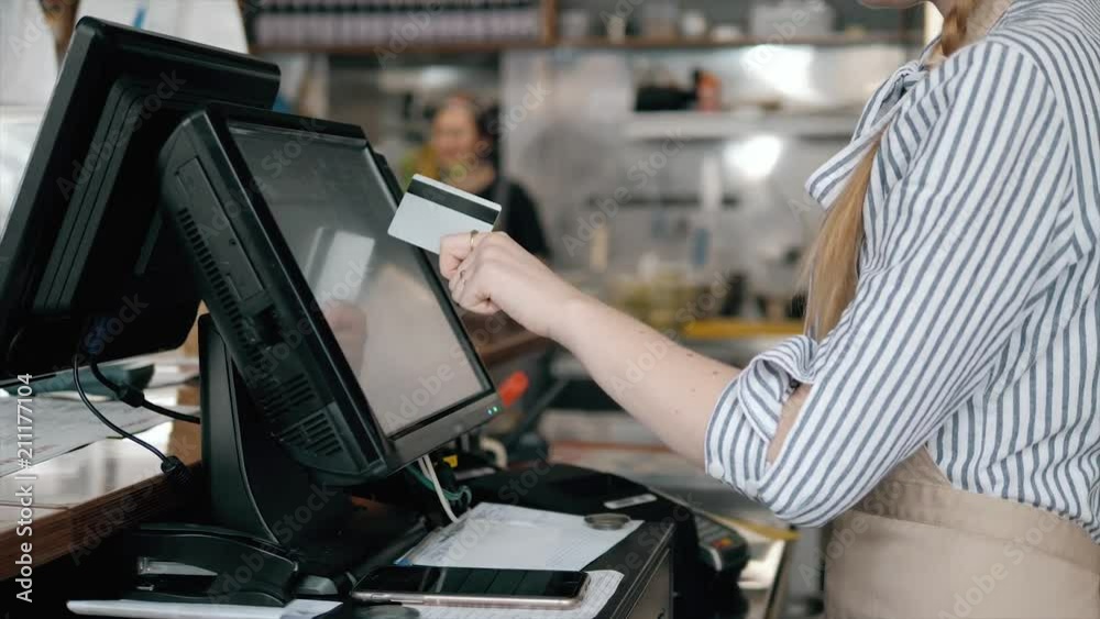 Side view of young bartender using modern cash register at bar counter ...