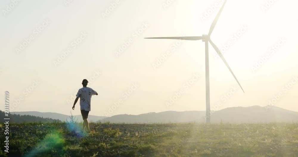 back view of male person looking at windmill blades rotating and then ...