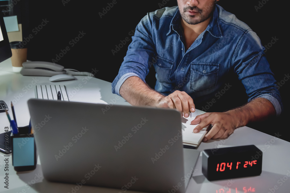 Workaholic man working on laptop computer late at night in the office ...