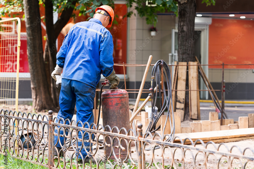 A man in a blue uniform and helmet unscrews the valve of the propane ...