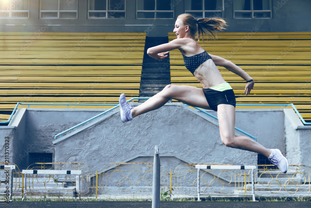 Athletic girl wearing sneakers and sport suit jumping above the hurdle ...