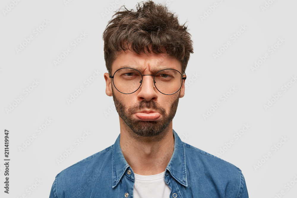 Discontent unshaven young Caucasian male purses lips and has miserable ...