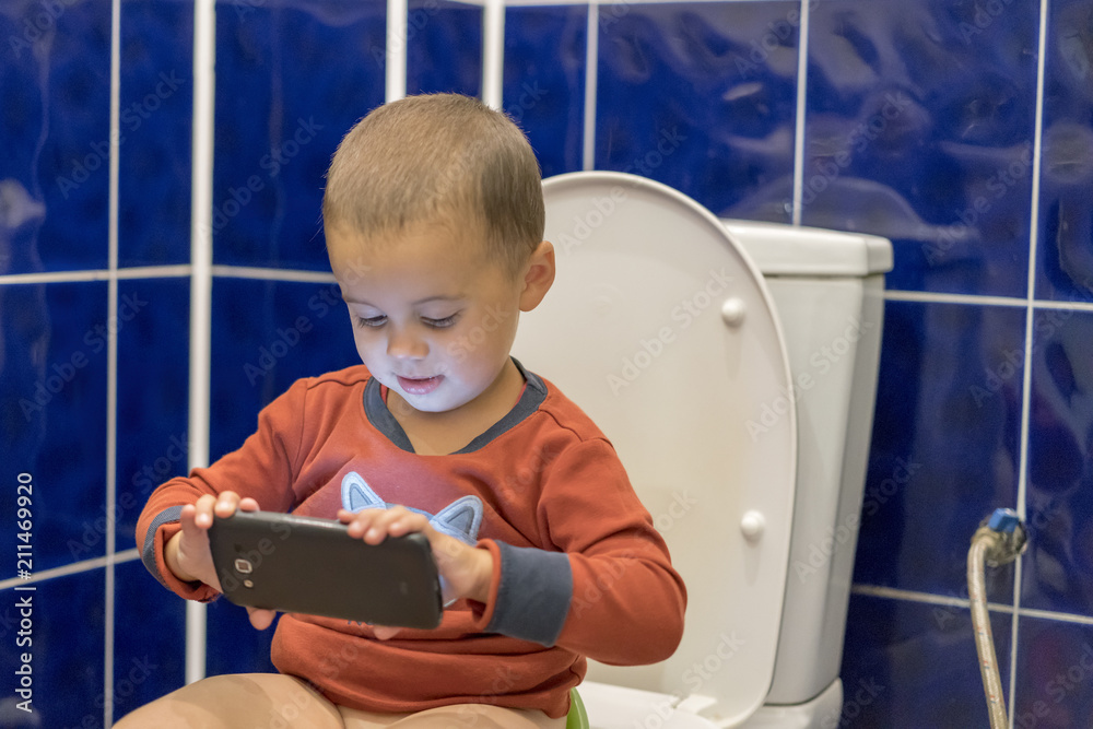 Cute toddler boy with smartphone in the bathroom. Little boy sitting on ...