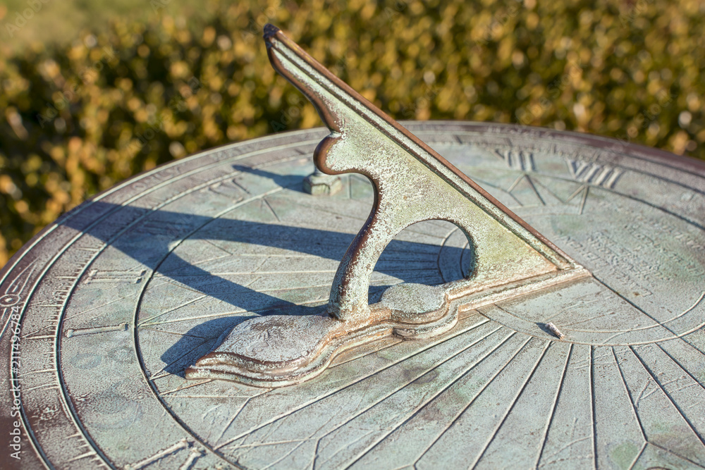 A vintage sundial with green patina throws a long shadow, tracking the ...