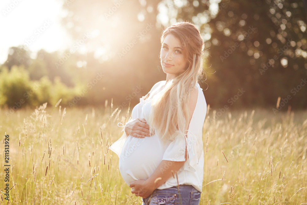 Lovely young future mother with long hair, keeps hands on her belly ...