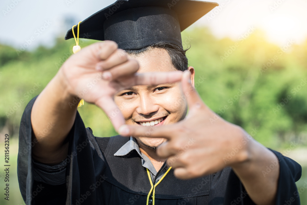 Handsome Graduated man in cap and gown smile and making finger frame ...