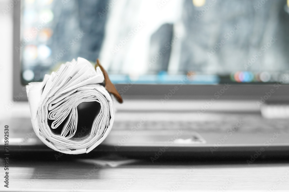 Computer and newspapers. Rolled papers with news on keyboard of laptop. Different sources of ...