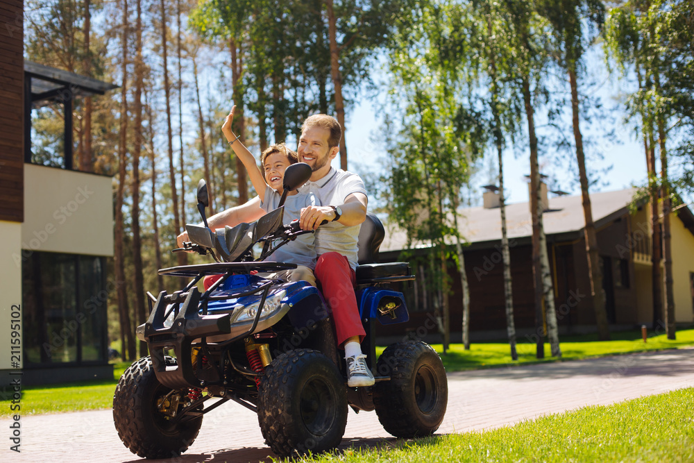 Best day. Happy young father smiling and driving an all-terrain vehicle ...