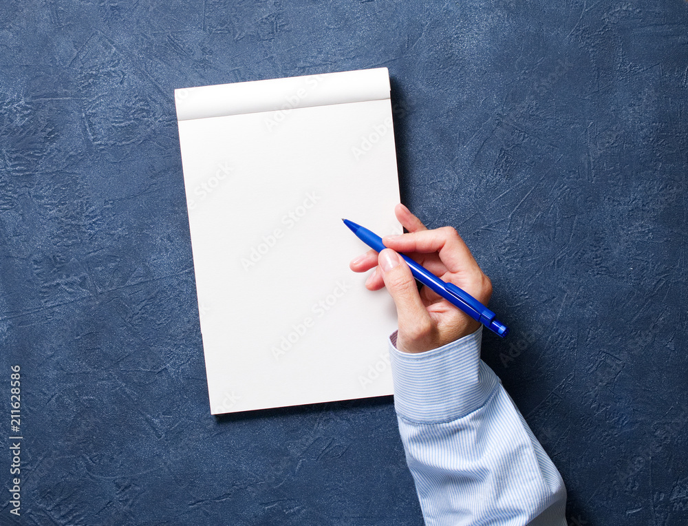woman writes in notebook on dark blue table, hand in shirt holding a ...