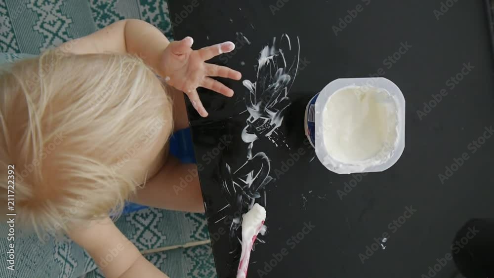 Baby eating yogurt making a mess. View from above shot of blond baby ...