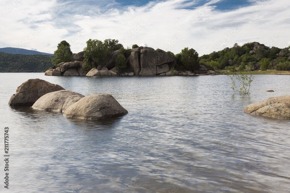 Vista de un lago con rocas en primer término y más rocas con árboles en ...