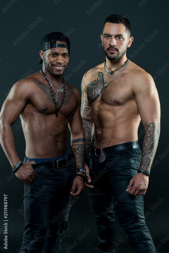 Friends with bare torsos wearing dark jeans. African and Caucasian men ...