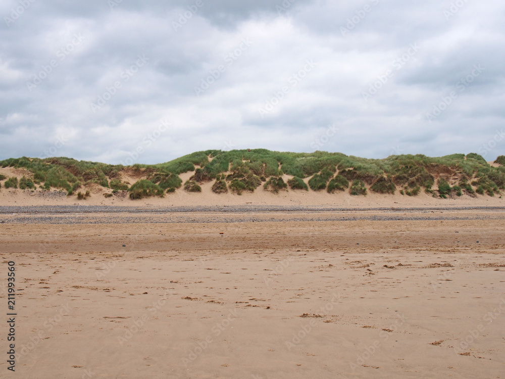 grassy sand dunes at the edge of a flat sandy beach with footprints in ...