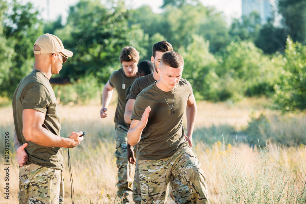 tactical instructor with stop watch examining multiracial soldiers ...
