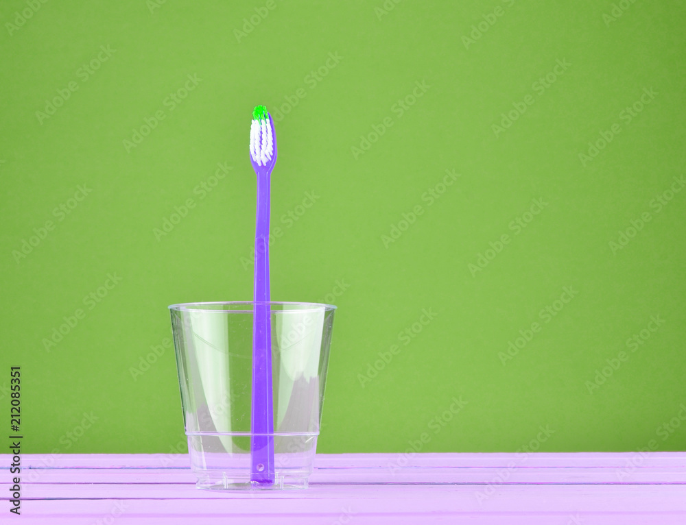 Pink toothbrush in a transparent cup on a minty green pastel background ...