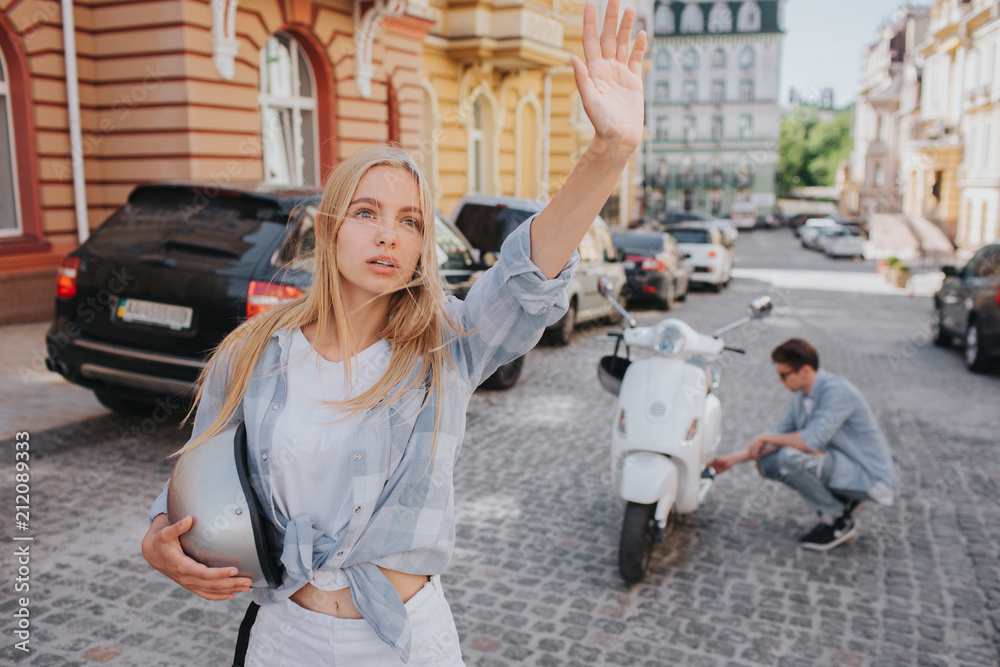 Girl is standing on road and waving with her hand. She is looking to ...