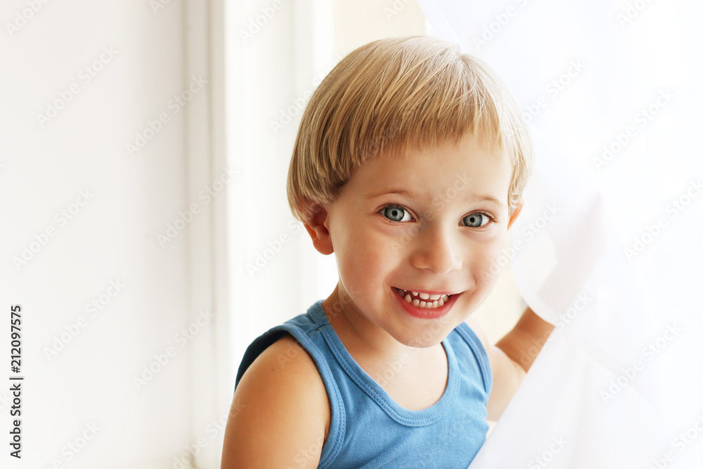 Cute little blond boy sitting on window sill, playing hide-and-seek ...