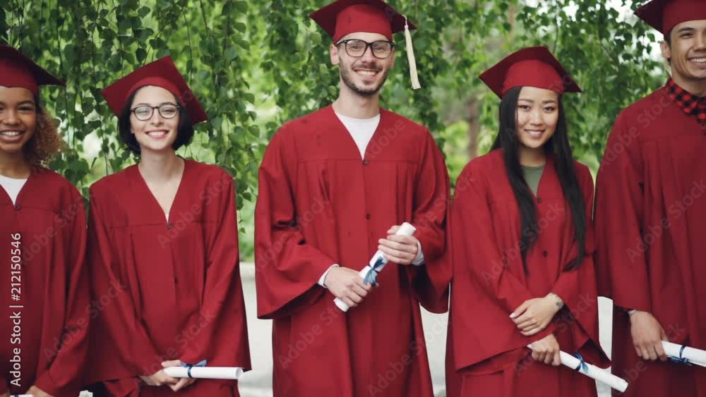 Dolly shot of smiling graduates standing in line on campus, looking at ...