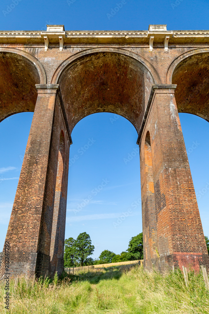 Looking up at the arches of the Ouse Valley Viaduct with a blue sky ...