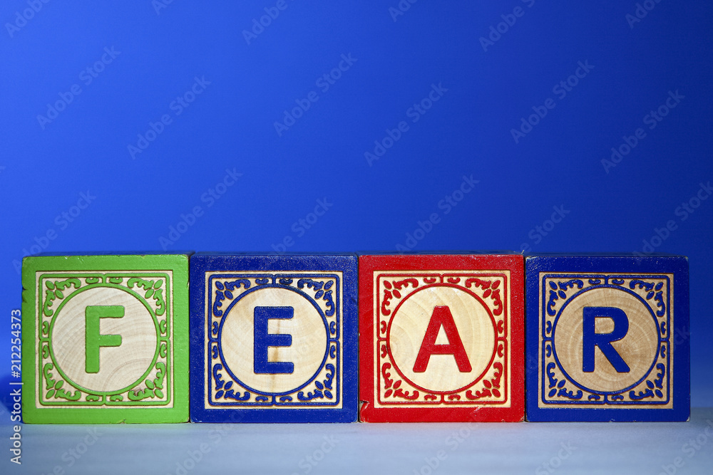 Wooden letter blocks on a blue background spelling out the word fear ...