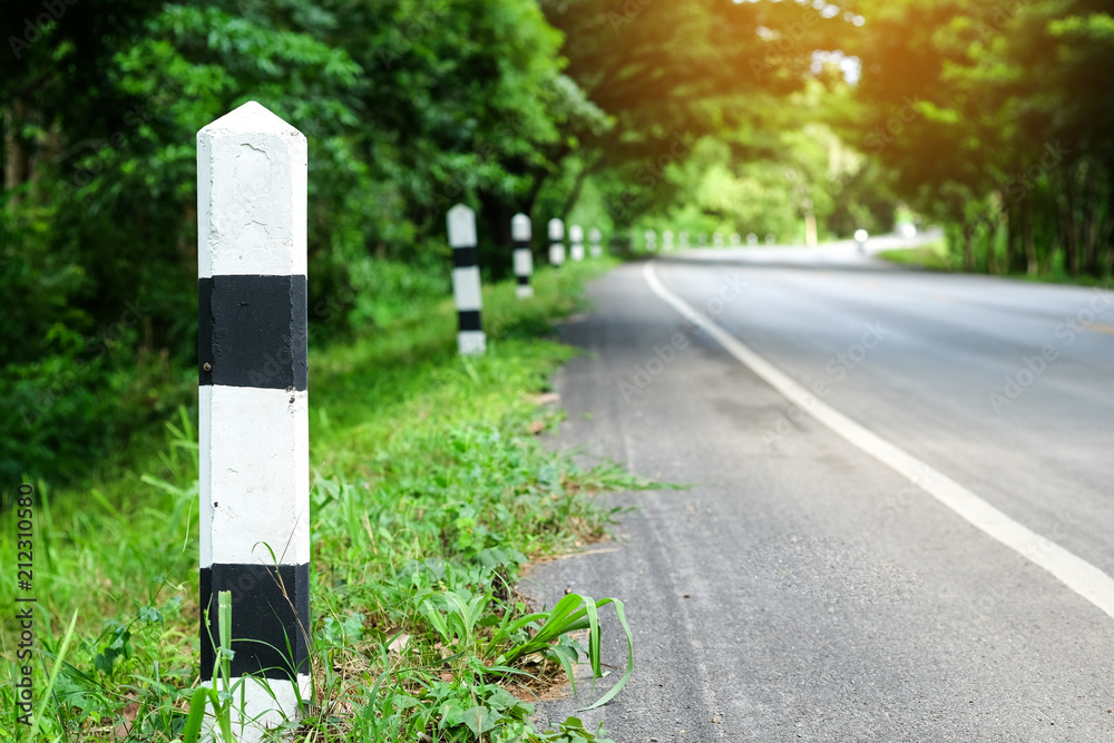 Black and white milestones with green grass roadside, Trees roadside in ...