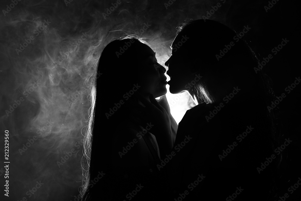 Silhouette Of Two Sexy Woman Kissing Holding In Darkness Through Light