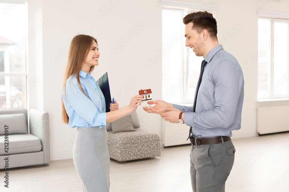 Beautiful real estate agent giving house model to young man indoors ...