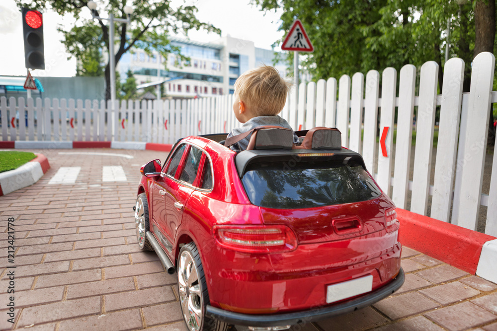 Little kid on a children's electric car is driving on special road for ...