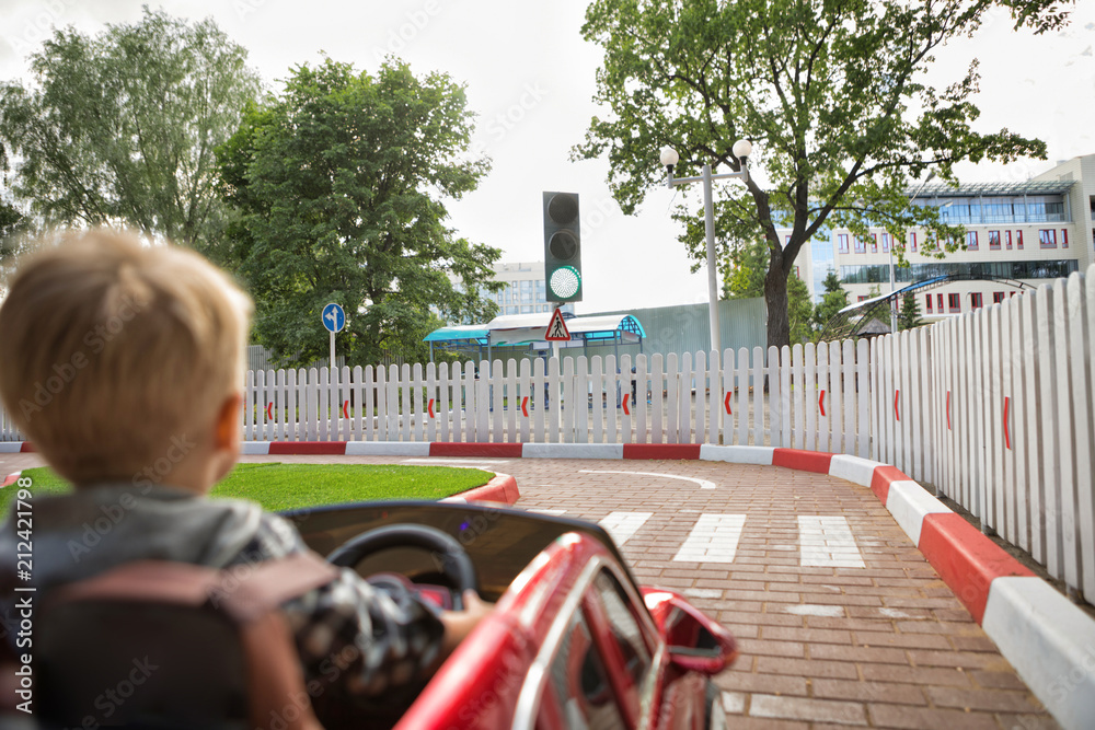 Little kid on a children's electric car is driving on special road for ...