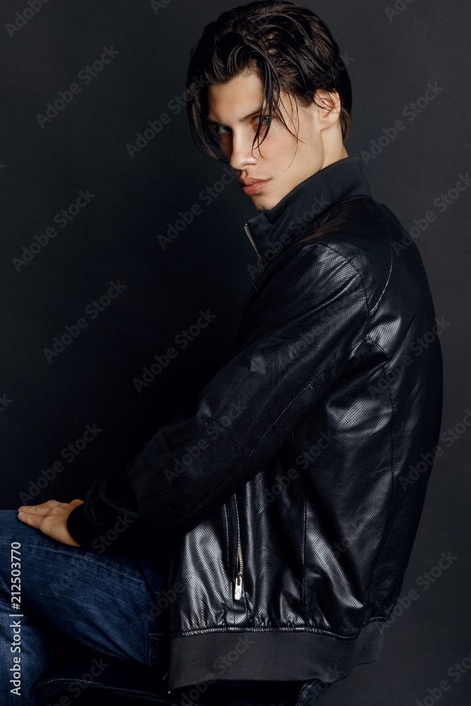 Male model in denim blue jeans and black leather jacket on black ...