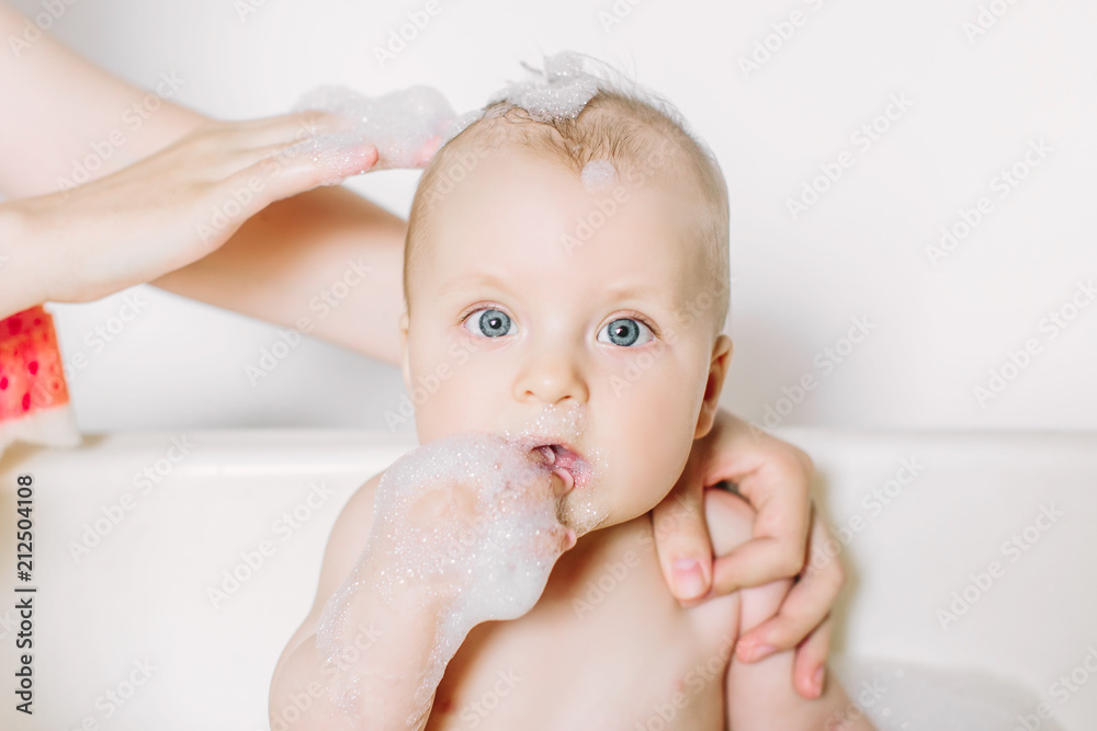 Happy laughing baby taking a bath playing with foam bubbles. Little ...