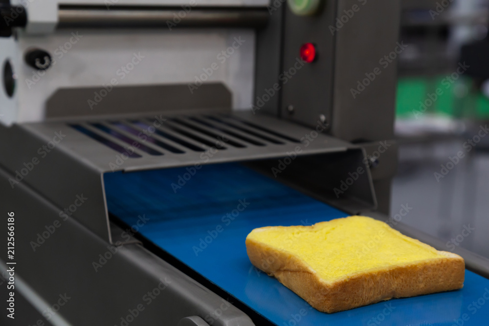 butter spread on fresh bread slice in production line on the conveyor ...