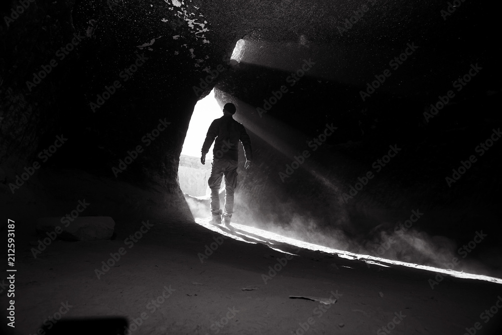 entrance to the cave, a male traveler stands in the rays of light at ...