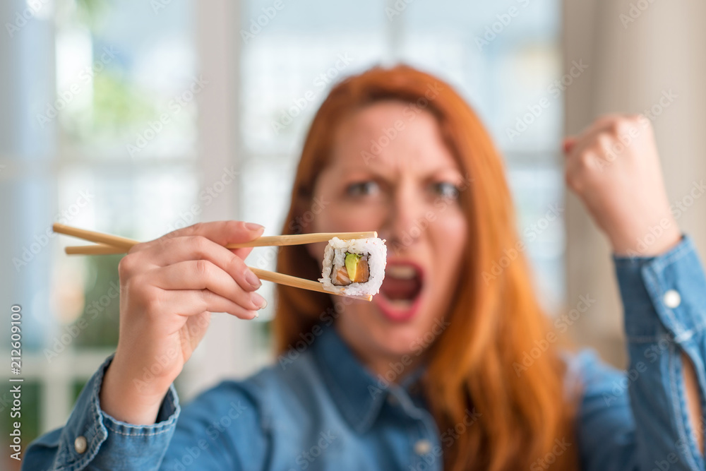 Redhead woman eating sushi using chopsticks annoyed and frustrated ...