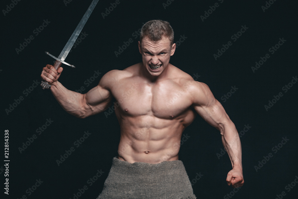 Bodybuilder man posing with a sword isolated on black background ...
