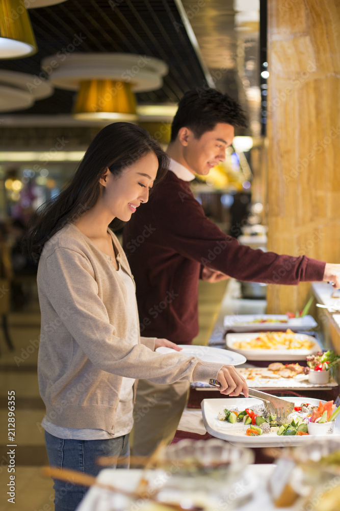Cheerful young Chinese couple taking food from buffet table Stock Photo ...