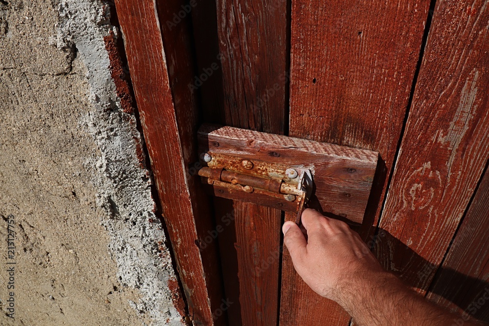Hand of adult man opening rusty bolt on wooden door of small concrete ...