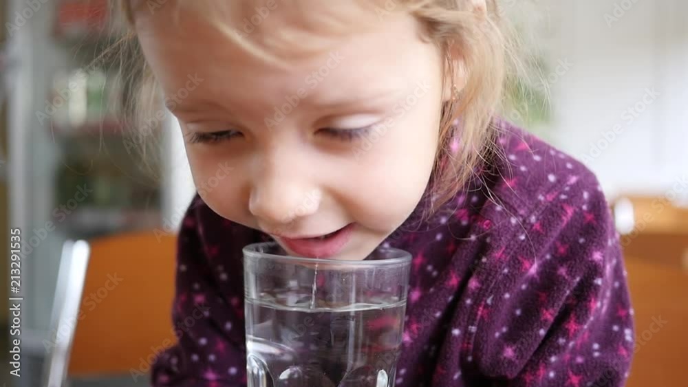 Little kid girl have fun drinking clear water lapping it with tongue in ...