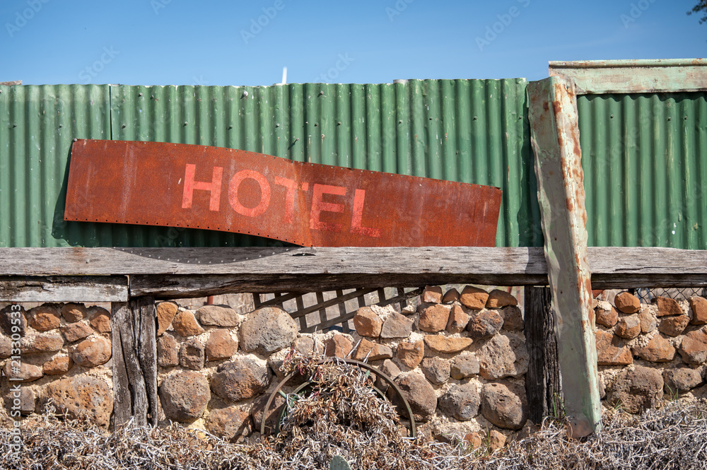 Old and rusted disused hotel sign leaning against a green corrugated ...