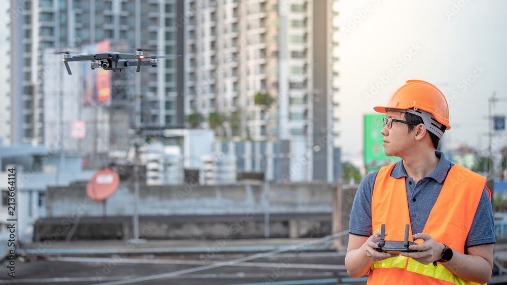 Young Asian engineer man flying drone over construction site. Using ...