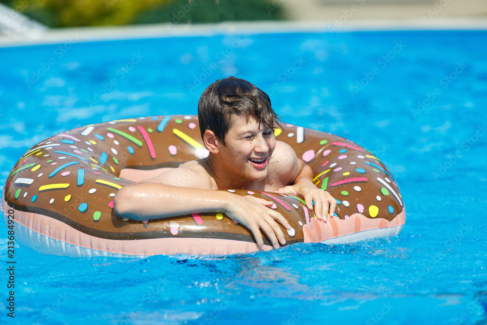 cute sporty boy swims in the pool with donut ring and has fun, smiles ...