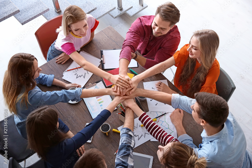 Young people putting hands together while working on project indoors ...