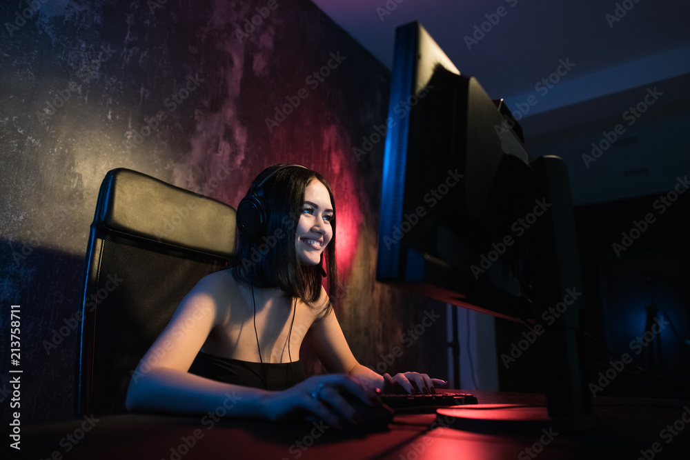 A cute female gamer girl sits in a cozy room behind a computer and ...