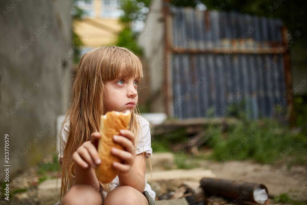 Portrait of hungry homeless girl eating a piece of bread in the dirty ...