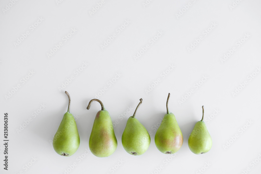 Five objects of green pears with twigs lie in a row on a white ...